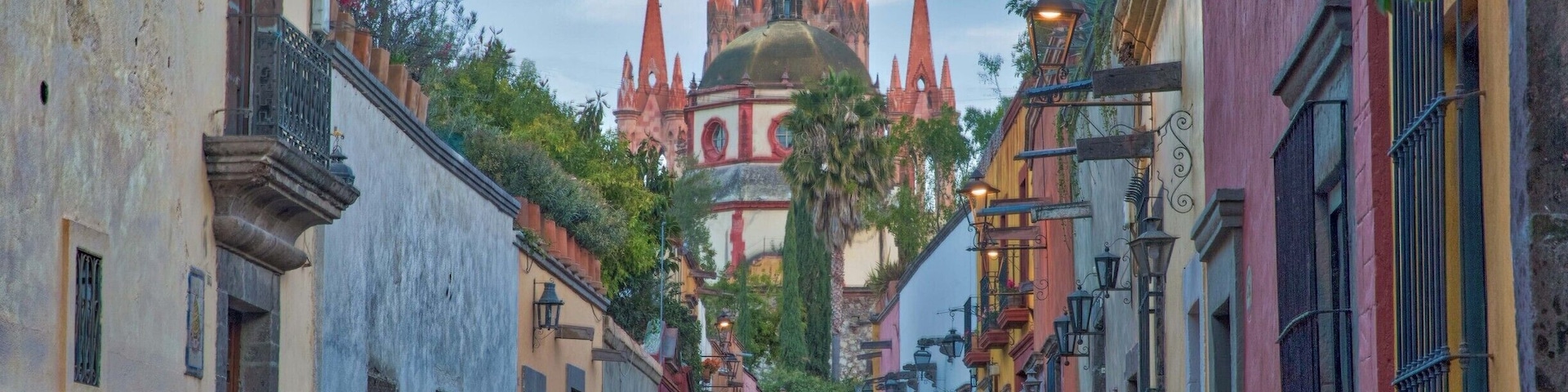 Uma rua de paralelepípedos ladeada por edifícios coloridos, uma igreja com uma torre alta e uma estátua de um homem carregando um escudo.