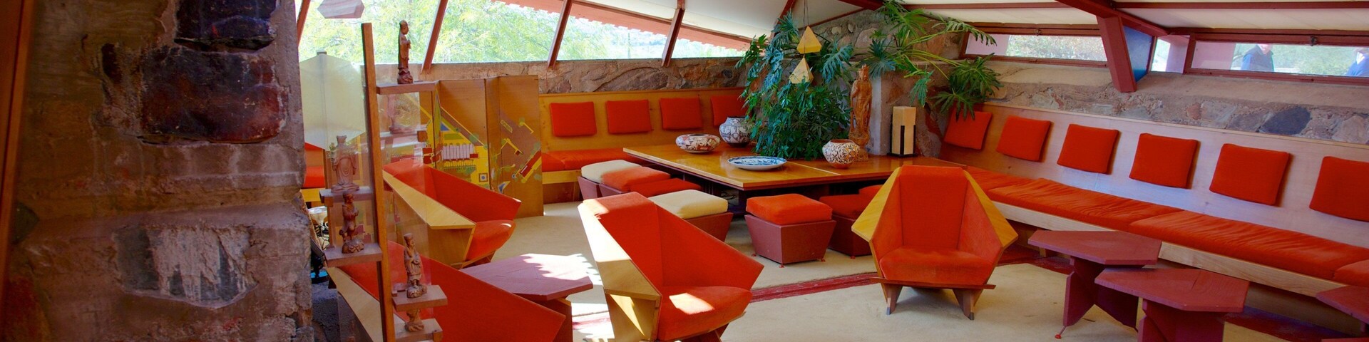 Um interior moderno com móveis laranja e vermelhos, uma parede de pedra e teto de madeira.