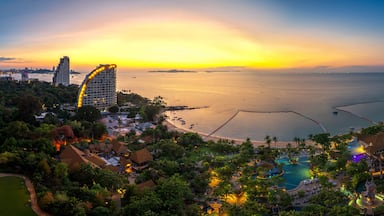 Um resort à beira-mar com uma piscina grande, palmeiras e um pôr do sol sobre a água.