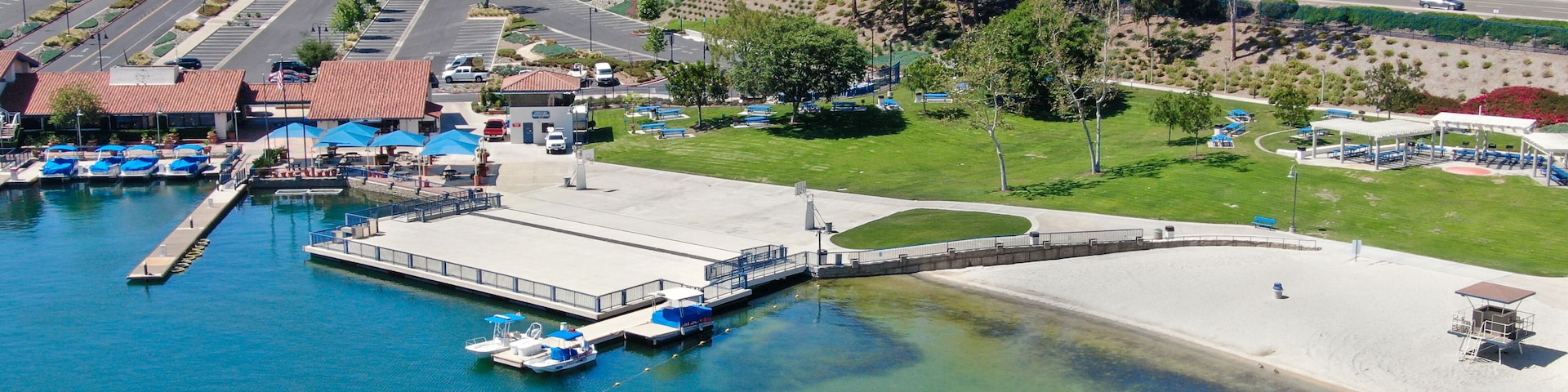 Uma marina com barcos, um estacionamento e uma cidade montanhosa ao fundo.