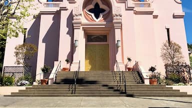 Uma igreja cor-de-rosa com uma torre central, duas torres laterais e uma grande cruz no topo.