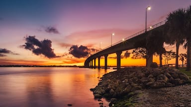 Ponte ao pôr do sol com um rio calmo e margem rochosa.